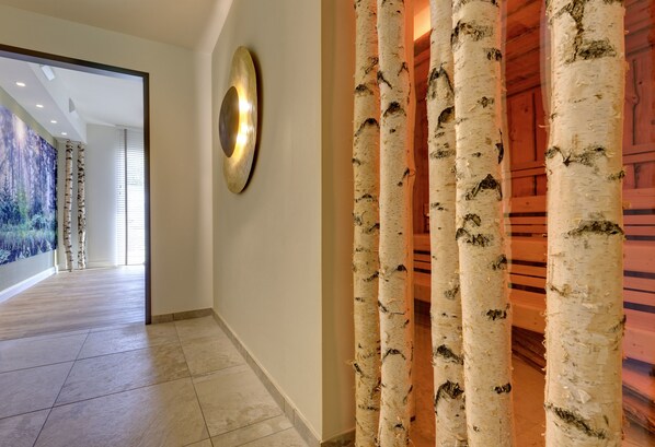 Um corredor com cortinas de madeira de bétula, um espelho circular fixado na parede e uma porta de madeira.