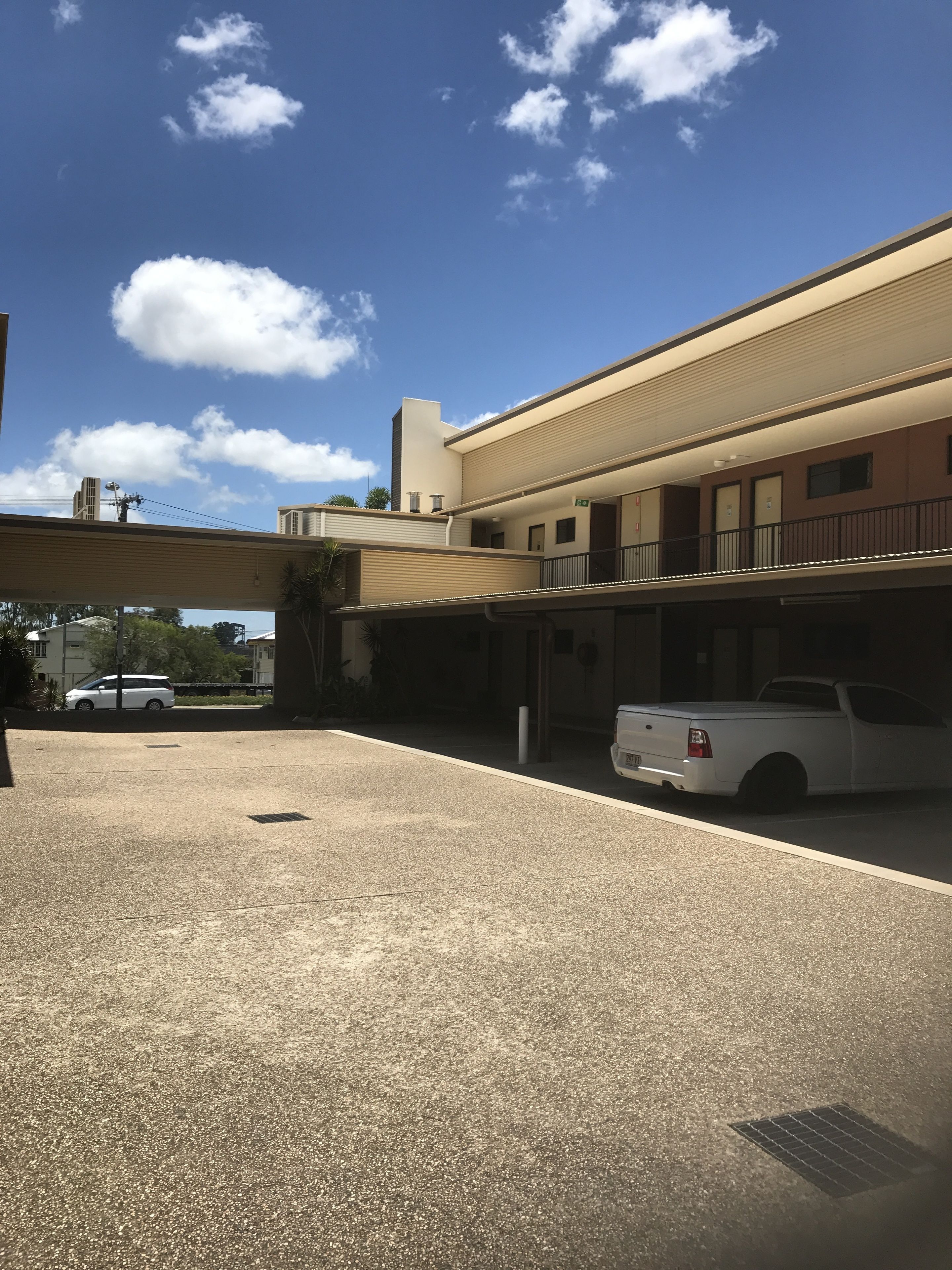 Uma área de estacionamento com um carro branco e um edifício com vários andares e varandas.