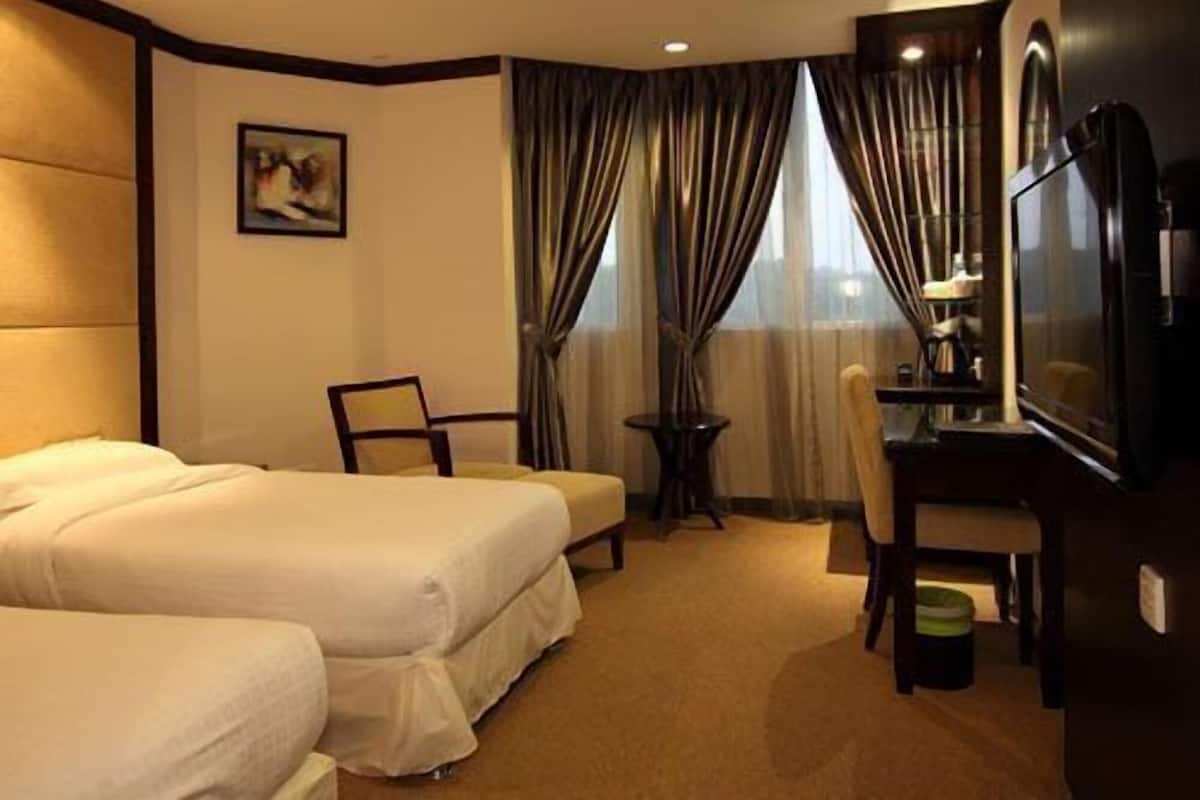 Quarto de hotel com duas camas, uma mesa, uma cadeira, televisão e janela com cortinas.