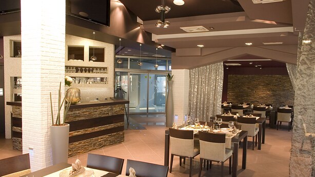 Restaurante com decoração moderna, incluindo um bar com copos e uma área de estar com mesas preparadas para refeições.