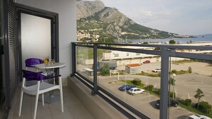 Varanda com mesa e cadeiras, com vista para um estacionamento e uma paisagem montanhosa.