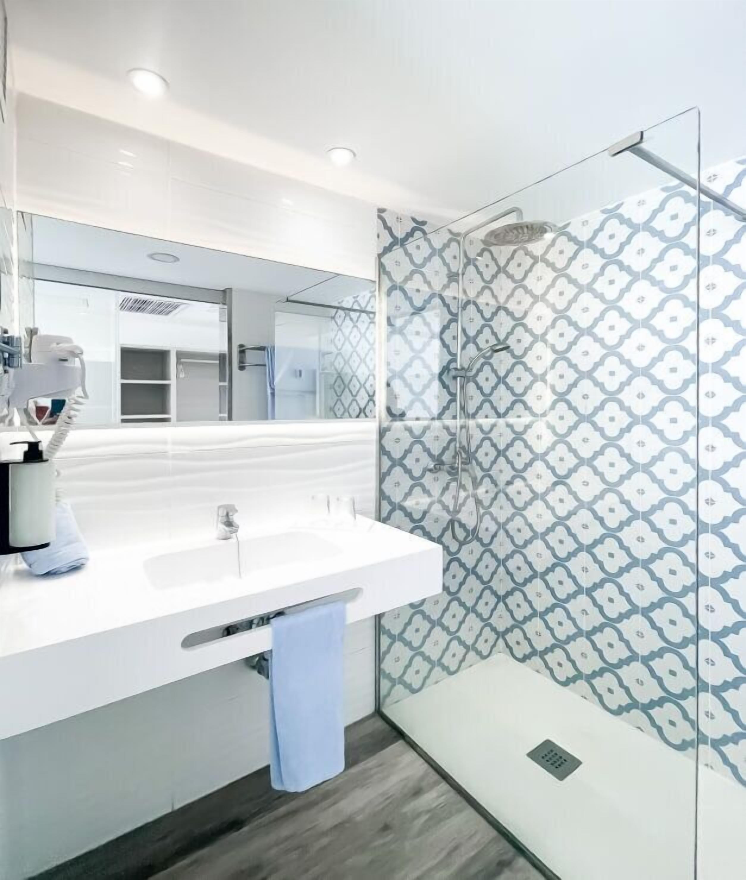 Uma casa de banho moderna com lavatório branco, cabine de duche em vidro e azulejos estampados.