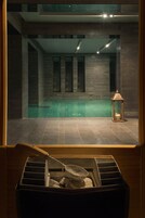 Piscina interior moderna com chão de pedra, um candeeiro e uma sauna com design vazado.