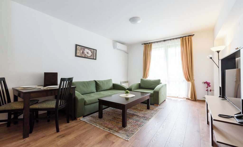 Uma sala de estar com um sofá verde, uma mesa de centro de madeira e uma área de jantar com cadeiras e mesa.