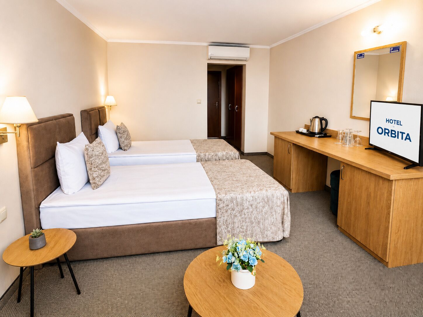 Quarto de hotel com duas camas, uma escrivaninha, televisão e uma pequena mesa com uma planta.