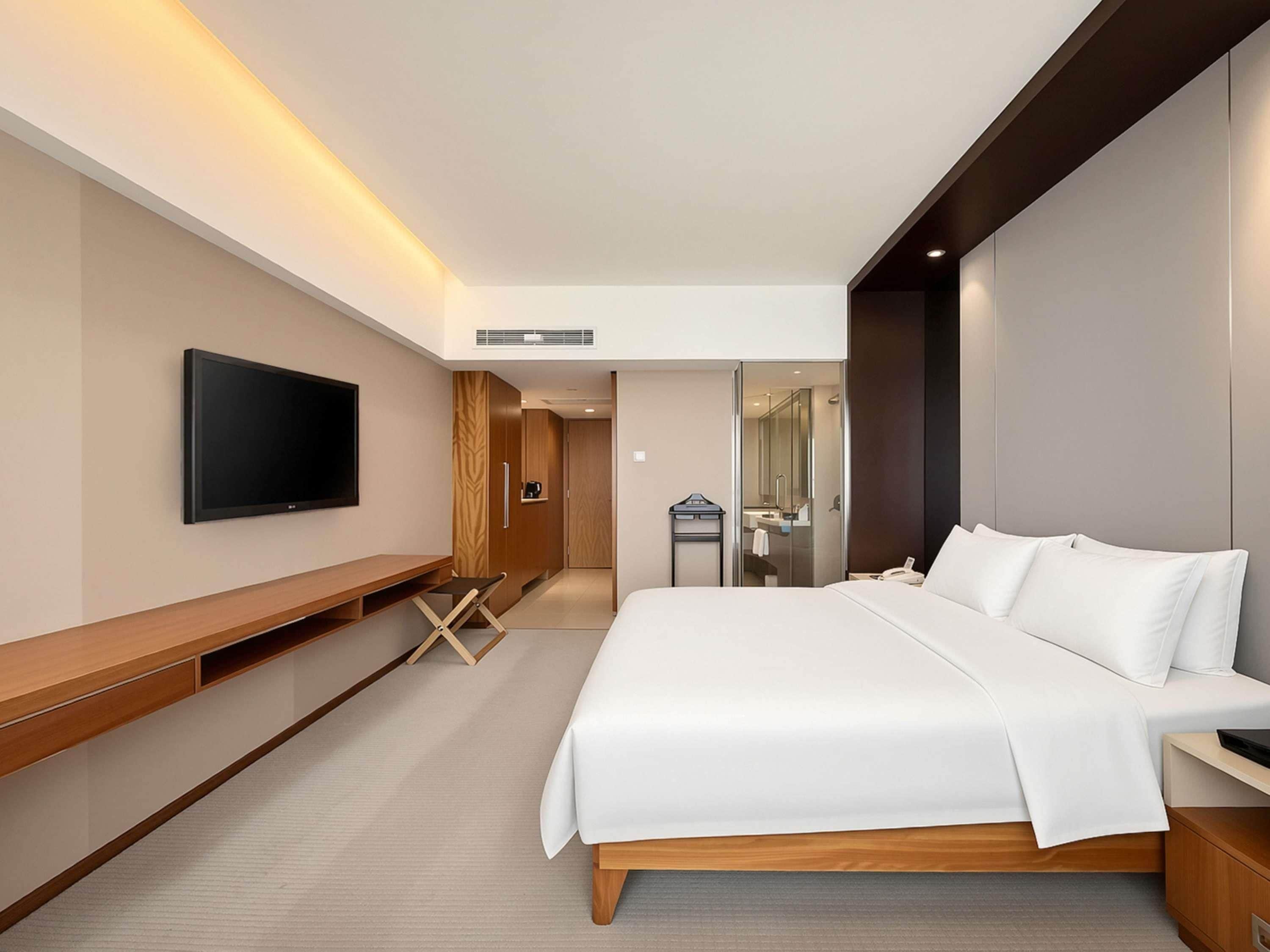Quarto de hotel moderno com uma cama grande, televisão de tela plana na parede, escrivaninha de madeira e closet espaçoso.