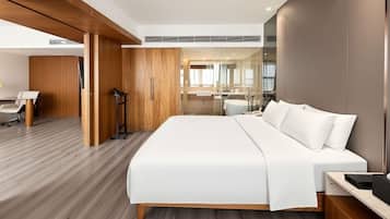 Quarto de hotel moderno com uma cama grande, uma escrivaninha, uma cadeira e um banheiro visível por meio de um painel de vidro.