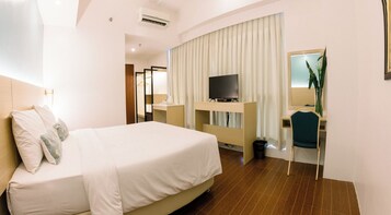 Quarto de hotel com uma cama grande, uma escrivaninha com televisão, uma cadeira e um espelho.