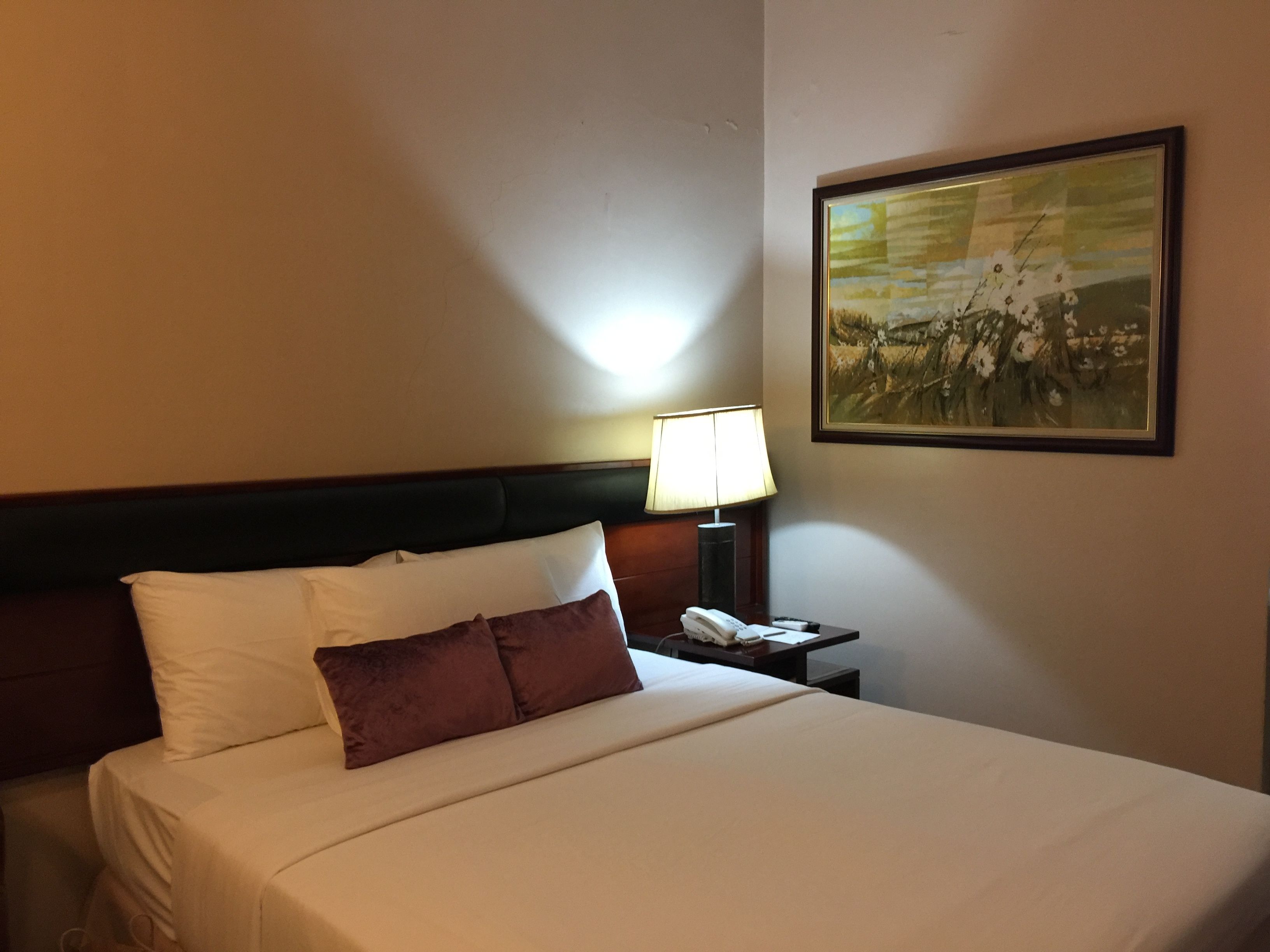 Quarto de hotel com cama bem arrumada, luminária de cabeceira, telefone e quadro na parede.
