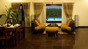 Quarto com duas poltronas, uma mesa de jantar com cadeiras, vista para um corpo de água e uma planta grande.