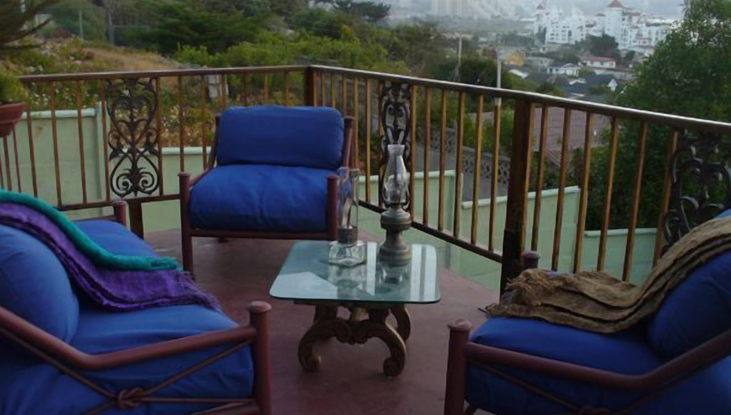 Uma varanda com duas cadeiras acolchoadas azuis, uma mesa pequena com um objeto decorativo e vista para um horizonte urbano.