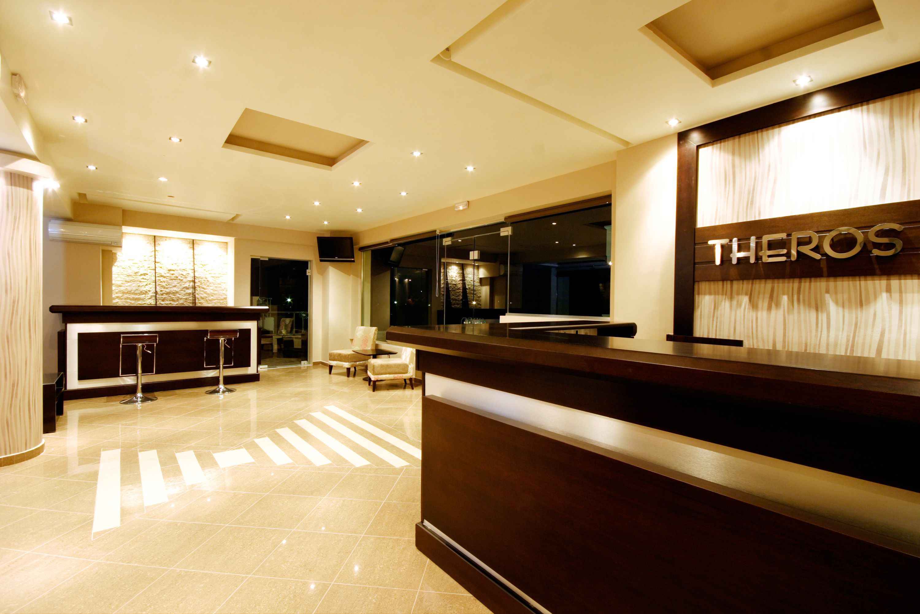 Uma área de recepção de hotel com balcão, espaço de estar e uma grande janela com cortinas.