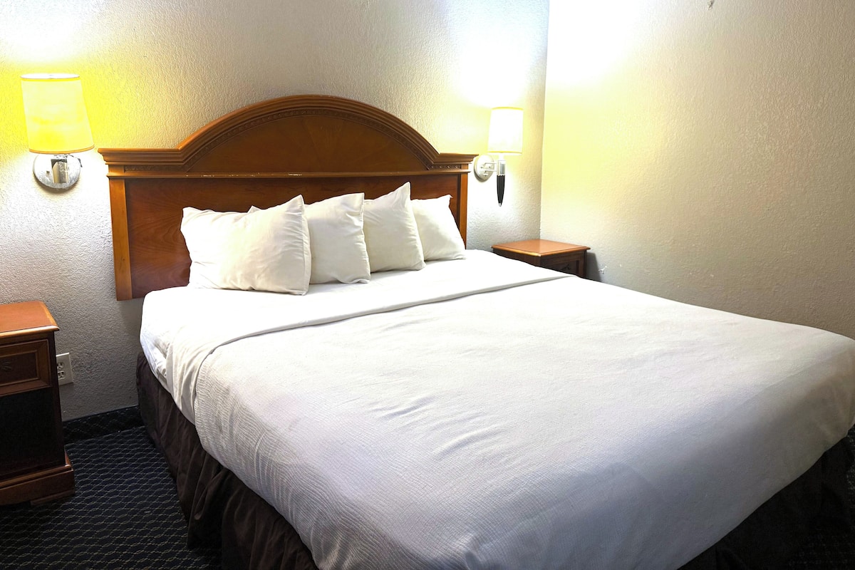 Cama bem arrumada com lençóis e almofadas brancas, duas luminárias de mesa e cabeceira de madeira.