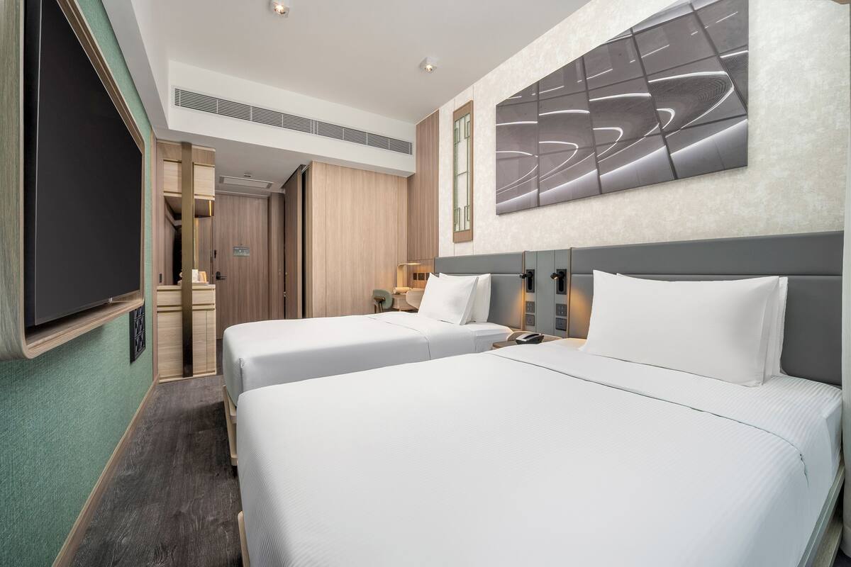 Quarto de hotel com duas camas, uma televisão de parede grande e design moderno.