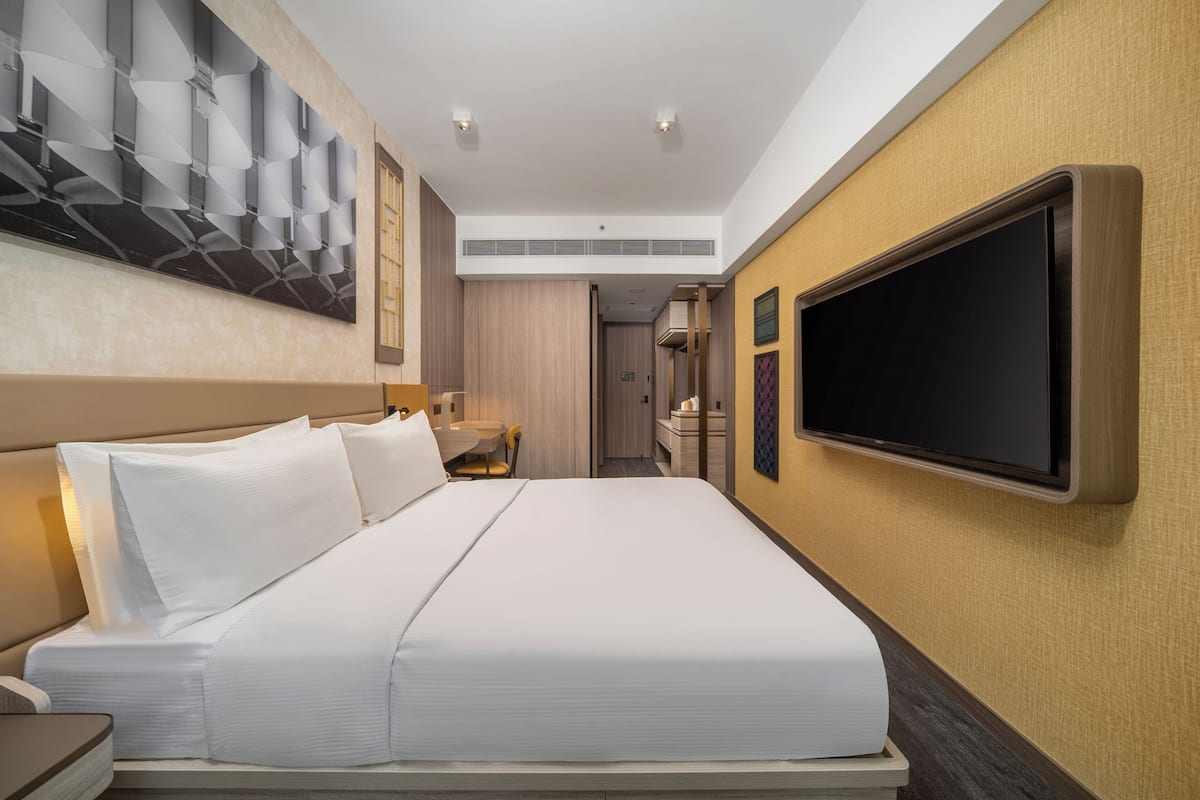 Quarto de hotel moderno com uma cama grande, uma TV de tela plana na parede e uma pequena escrivaninha com cadeira.