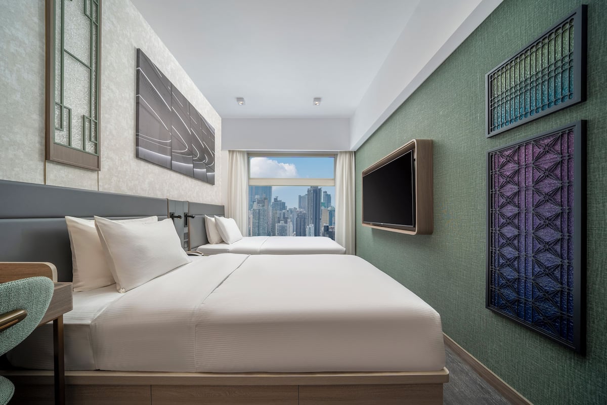 Quarto de hotel com uma cama grande, escrivaninha, cadeira, televisão e vista para a cidade.