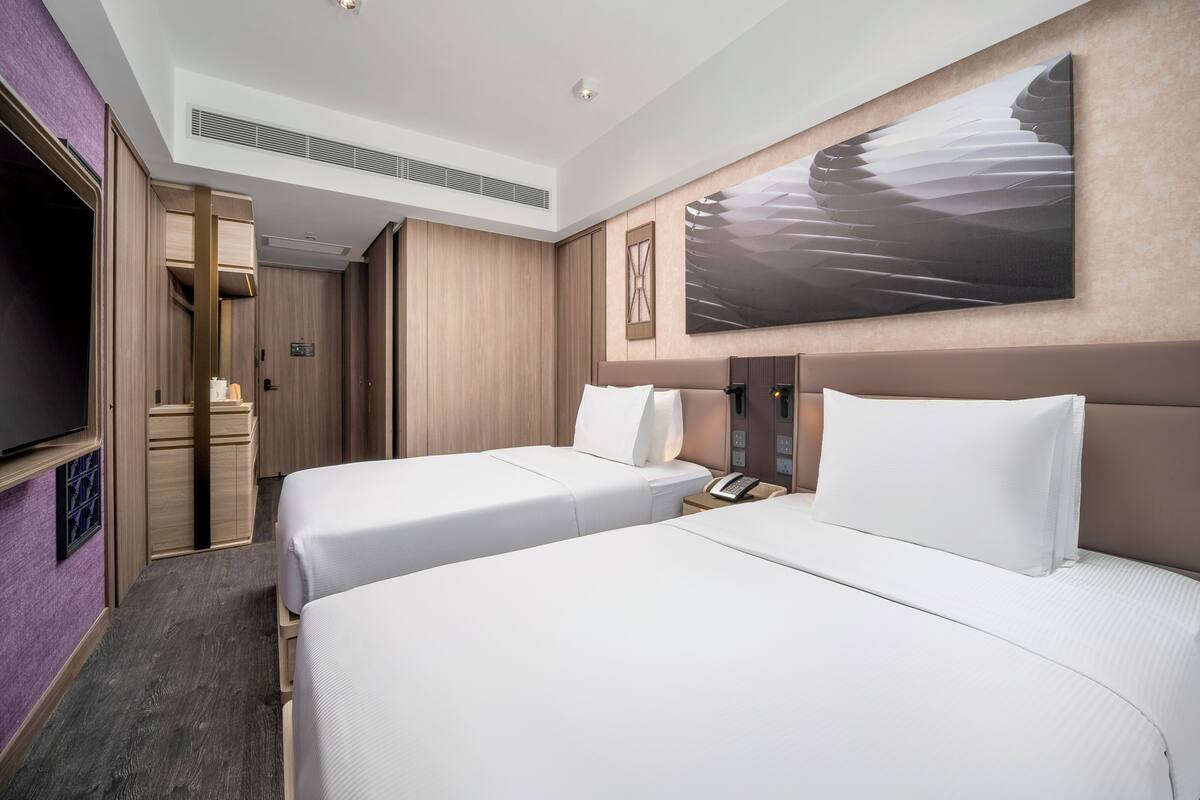 Quarto de hotel com duas camas, uma obra de arte grande fixada na parede, televisão de tela plana e guarda-roupa de madeira.