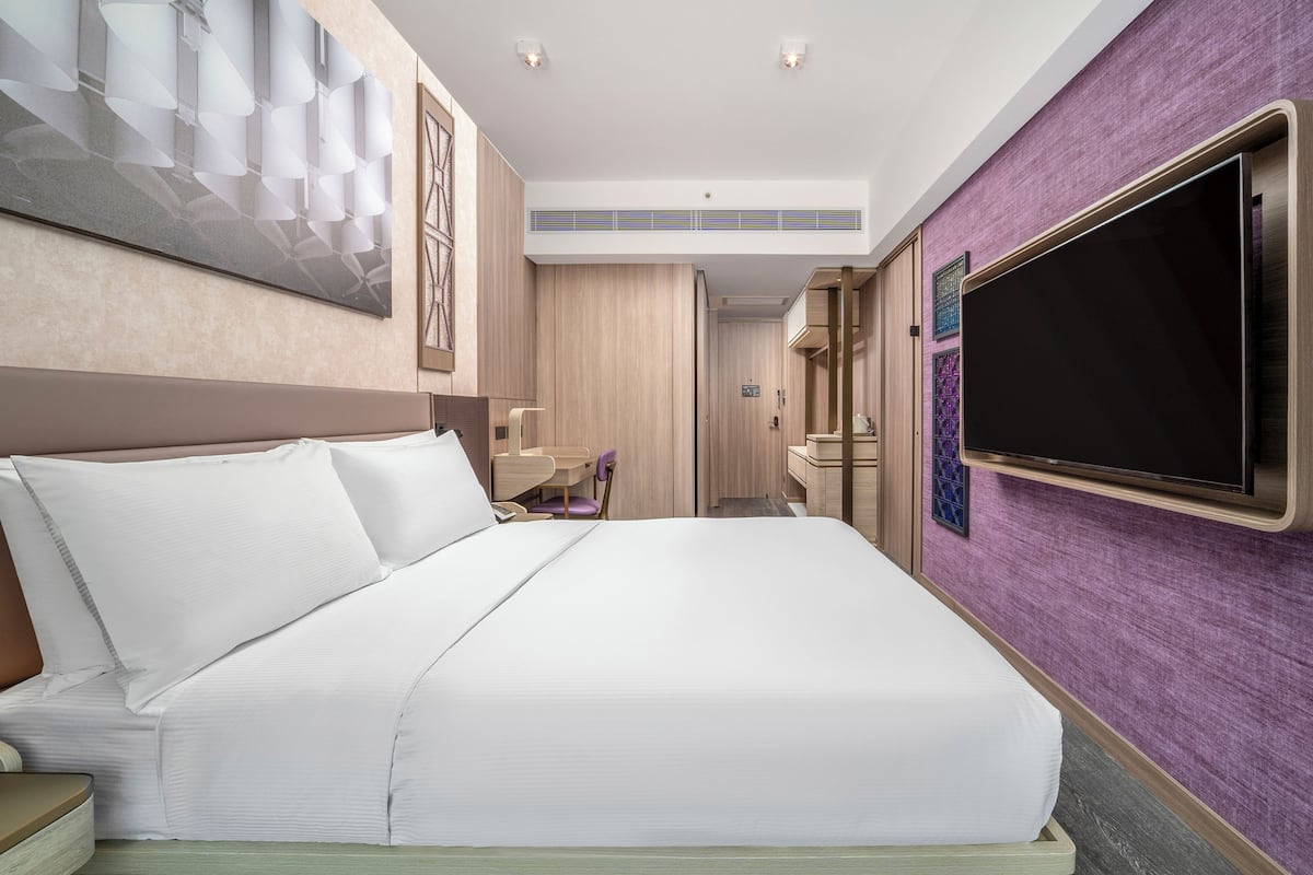 Quarto de hotel moderno com uma cama grande, televisão de tela plana, escrivaninha e uma cadeira.