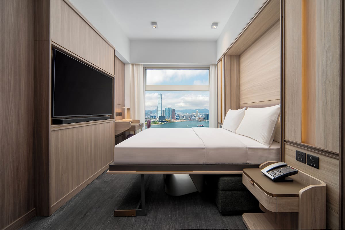 Quarto de hotel moderno com uma cama grande, televisão de tela plana, escrivaninha com telefone e vista para o horizonte da cidade.