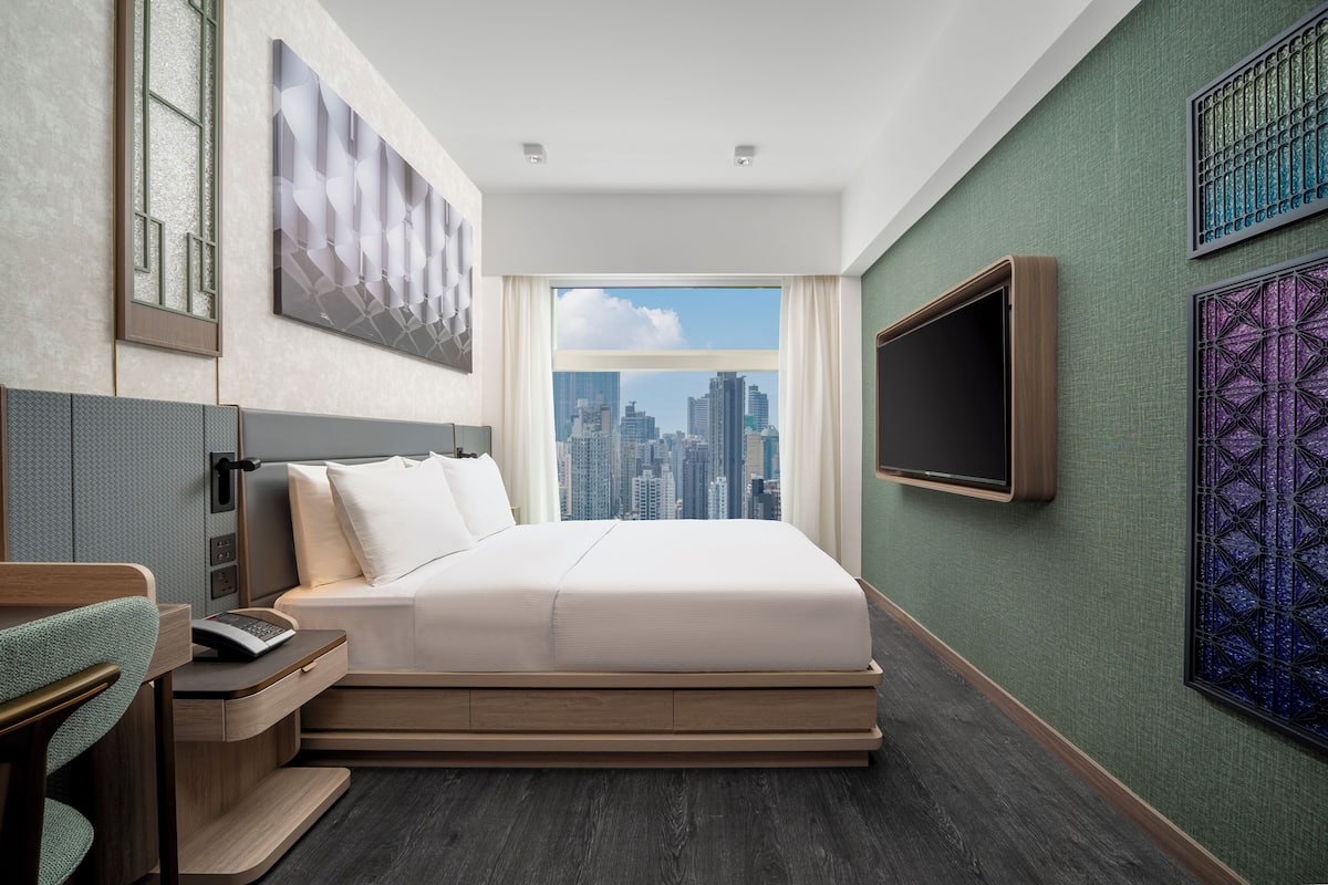 Quarto de hotel moderno com vista para a cidade, uma cama, uma escrivaninha e uma televisão.
