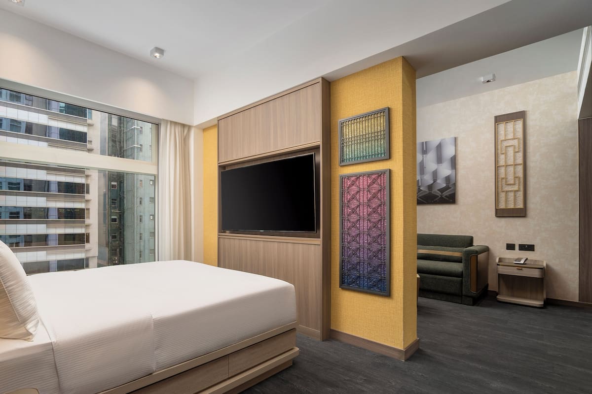 Quarto de hotel moderno com cama, televisão de tela plana, sofá e obras de arte nas paredes.