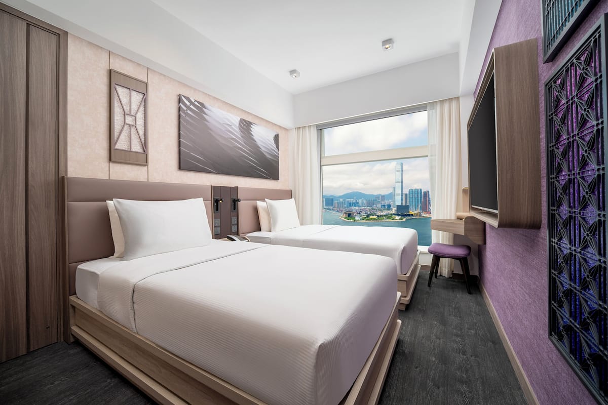 Quarto de hotel com duas camas, uma escrivaninha e uma janela grande com vista para a cidade.