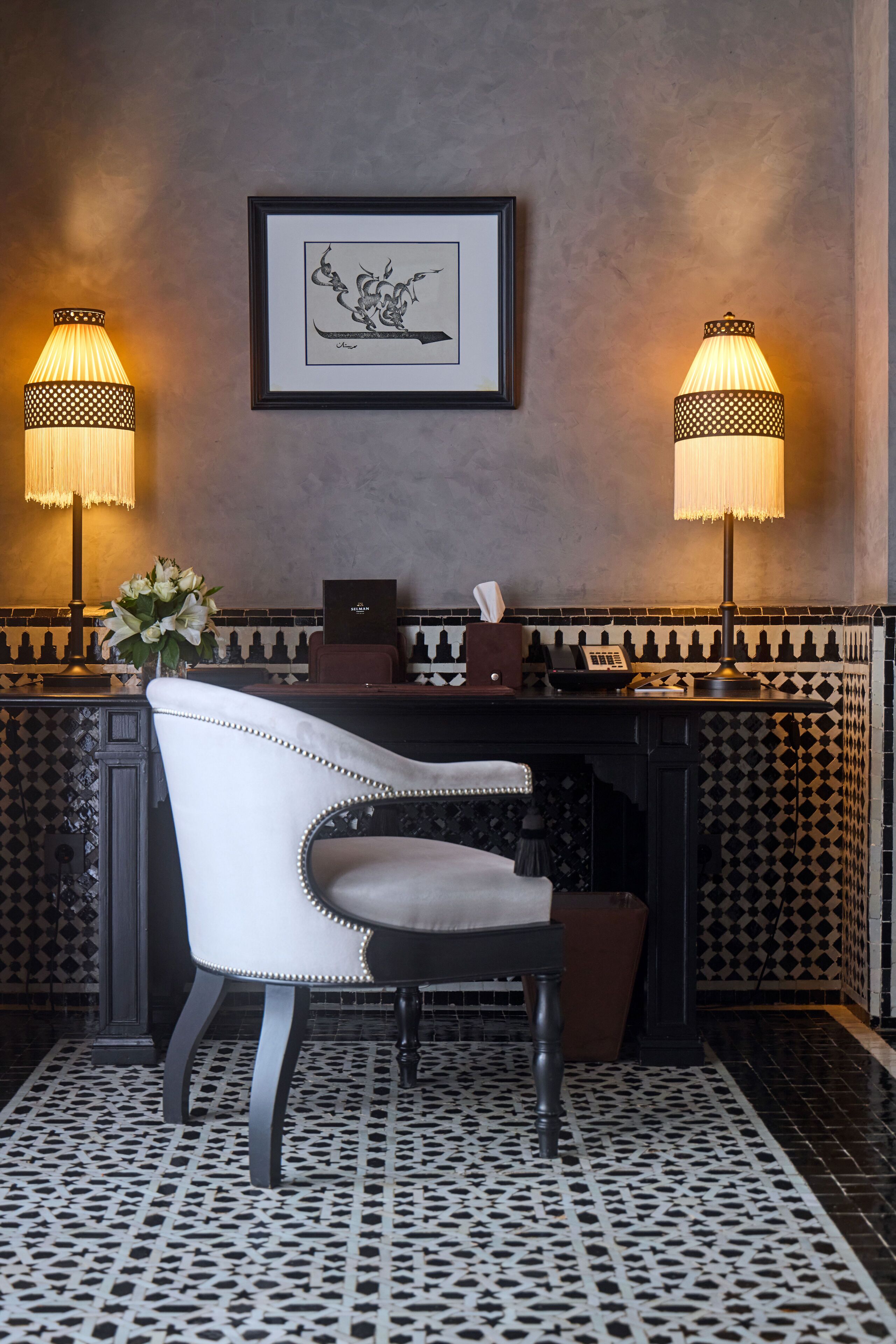 Uma mesa de recepção com duas luminárias, uma obra de arte emoldurada e um piso estampado.