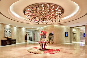 Um hall amplo com uma peça decorativa central, piso de mármore e design moderno no teto.