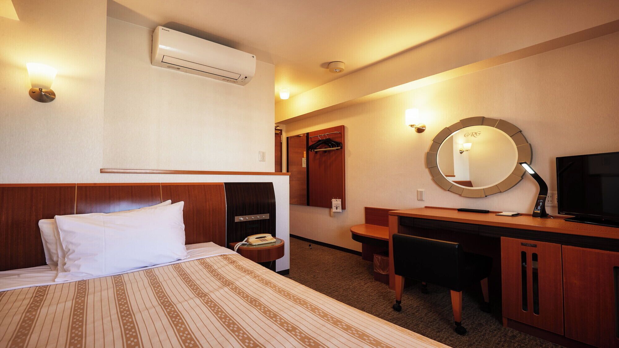 Quarto de hotel com cama, escrivaninha, televisão e espelho.