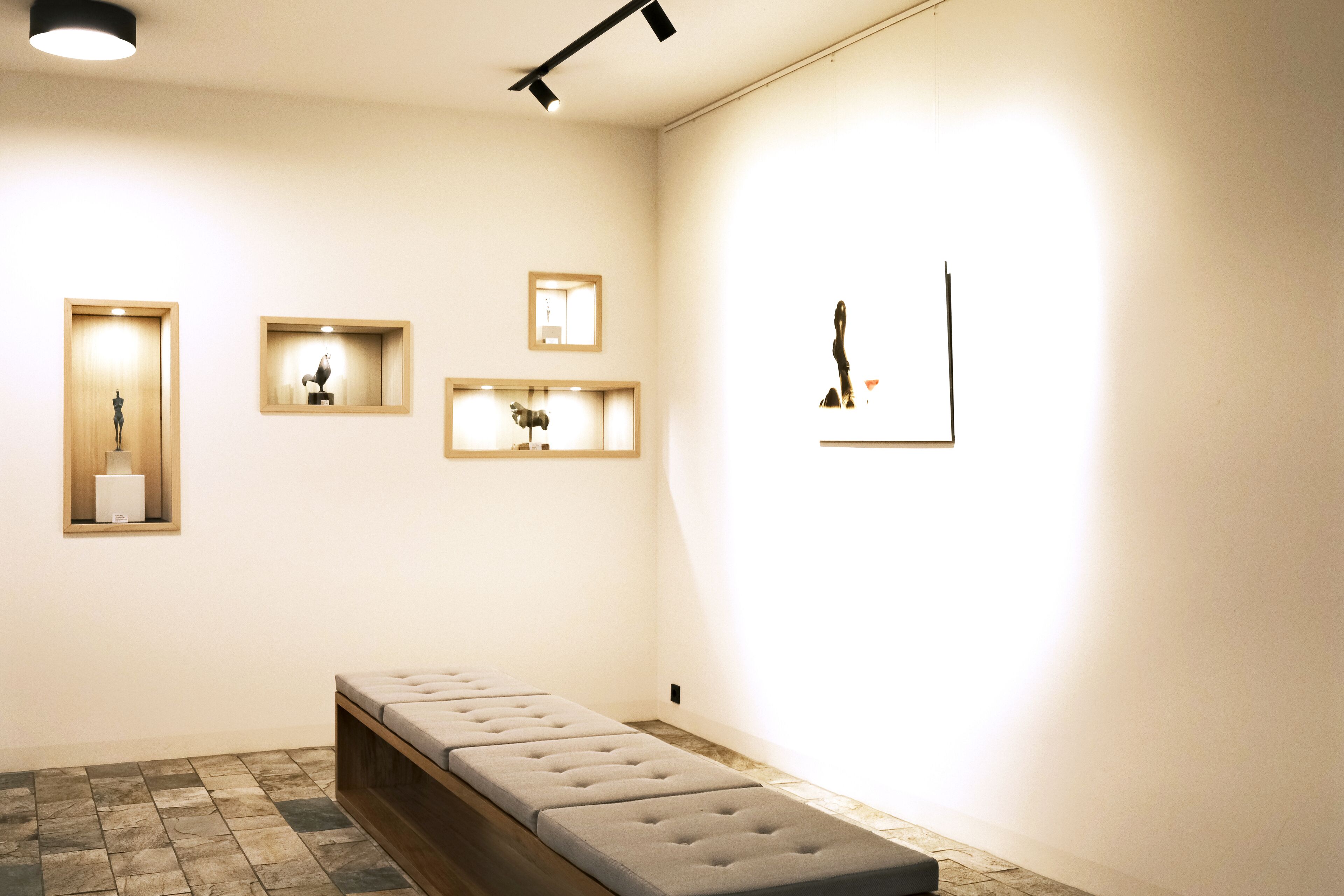 Quarto com um longo banco, prateleiras fixas na parede com esculturas e uma grande obra de arte emoldurada.