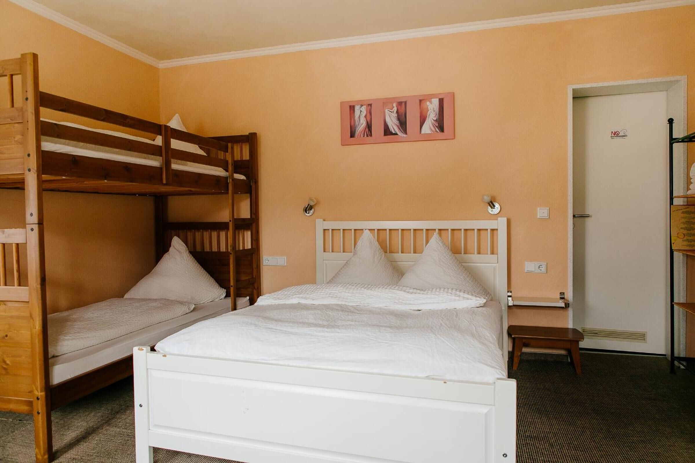 Quarto com beliches, uma cama de solteiro, uma mesinha de cabeceira e um quadro pendurado na parede.