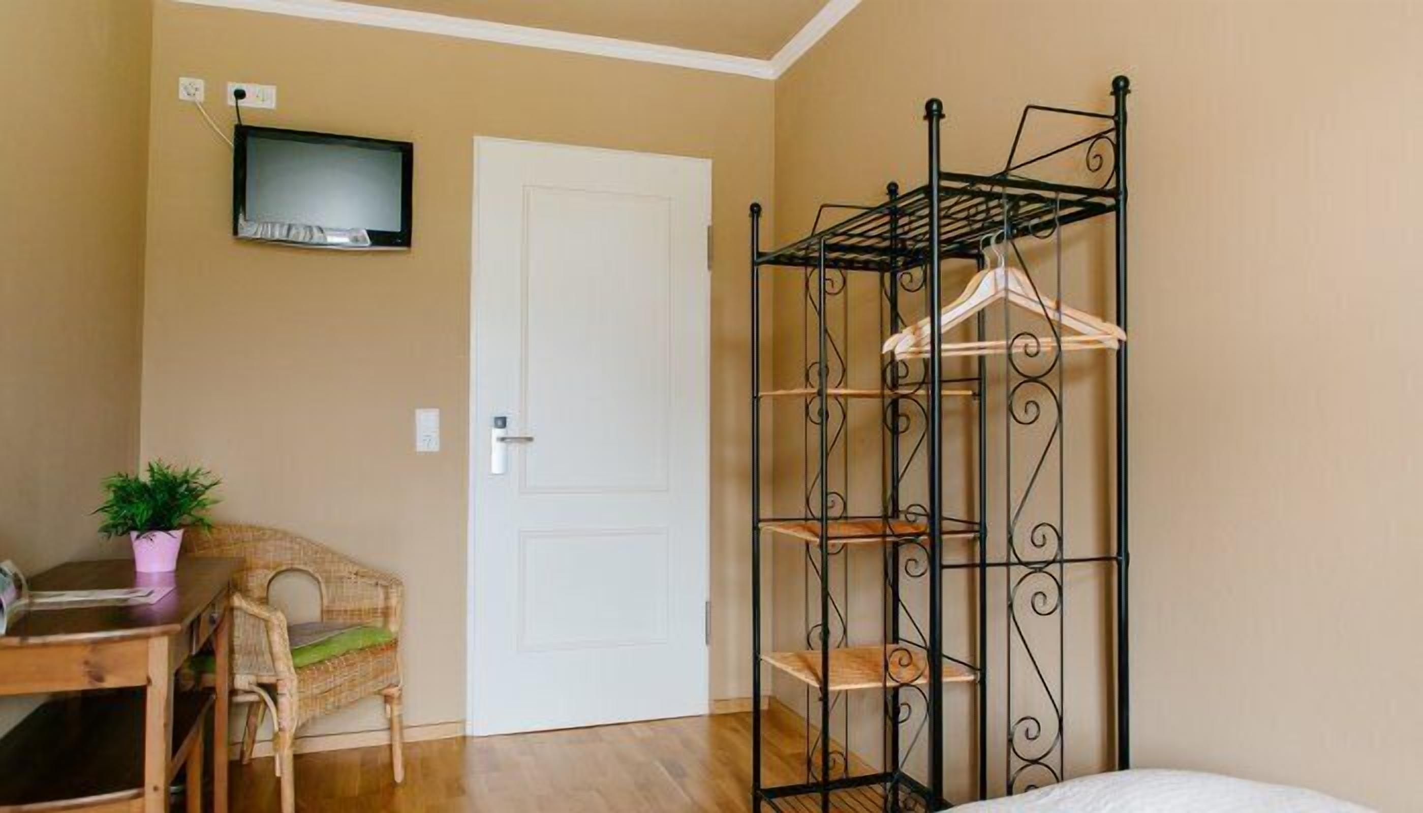 Quarto com cama, escrivaninha e cadeira, televisão na parede e guarda-roupa de metal com prateleiras.