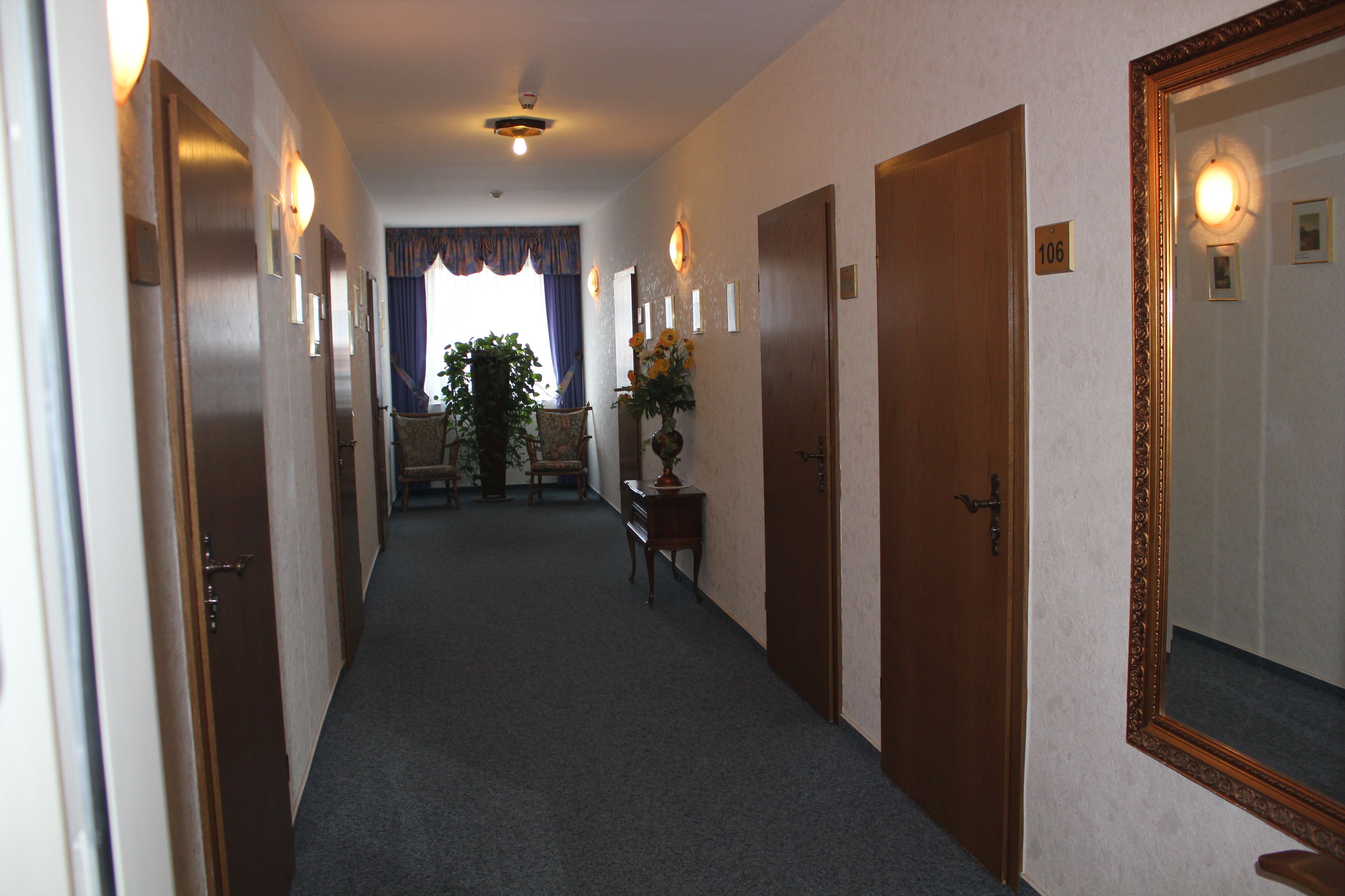 Corredor de hotel com portas, um espelho e uma planta.