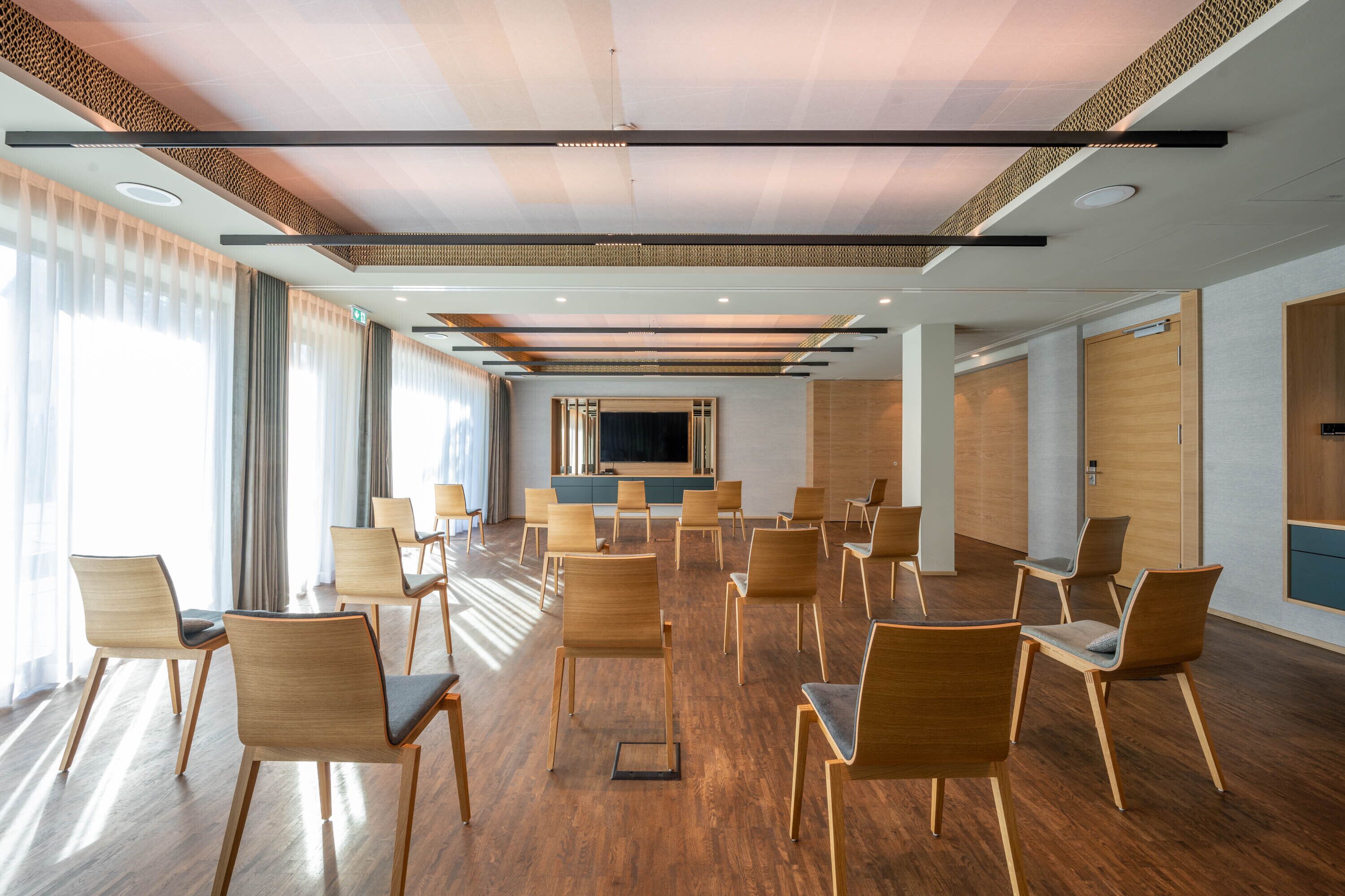 Uma sala de conferência com cadeiras de madeira dispostas em fileiras, uma tela grande na frente e um design de teto moderno.