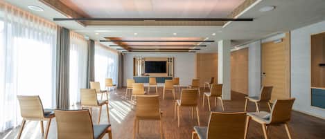 Uma sala de conferência com cadeiras de madeira dispostas em fileiras, uma tela grande na frente e um design de teto moderno.