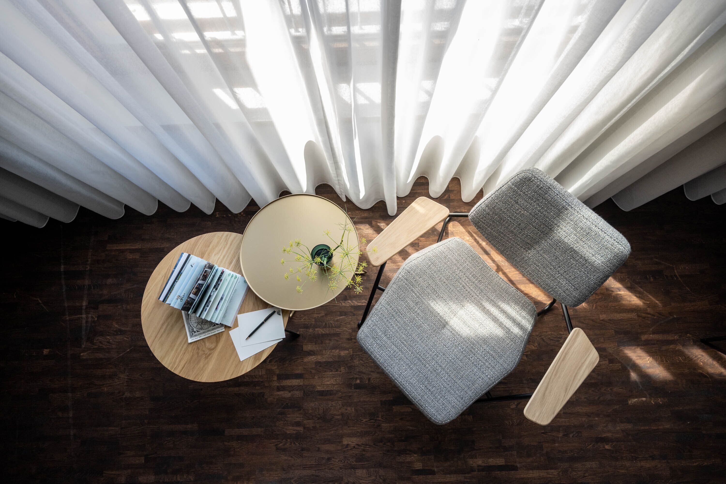 Quarto moderno com uma mesa de madeira redonda, uma cadeira estofada cinza e um vaso com planta.