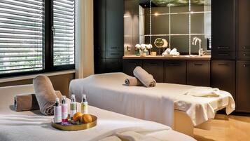 Um quarto de spa com duas camas, uma janela com persianas, uma toucador com produtos de higiene pessoal e um espelho com iluminação.