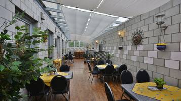 Um restaurante com mesas e cadeiras, piso de madeira e parede de tijolos com decoração solar.