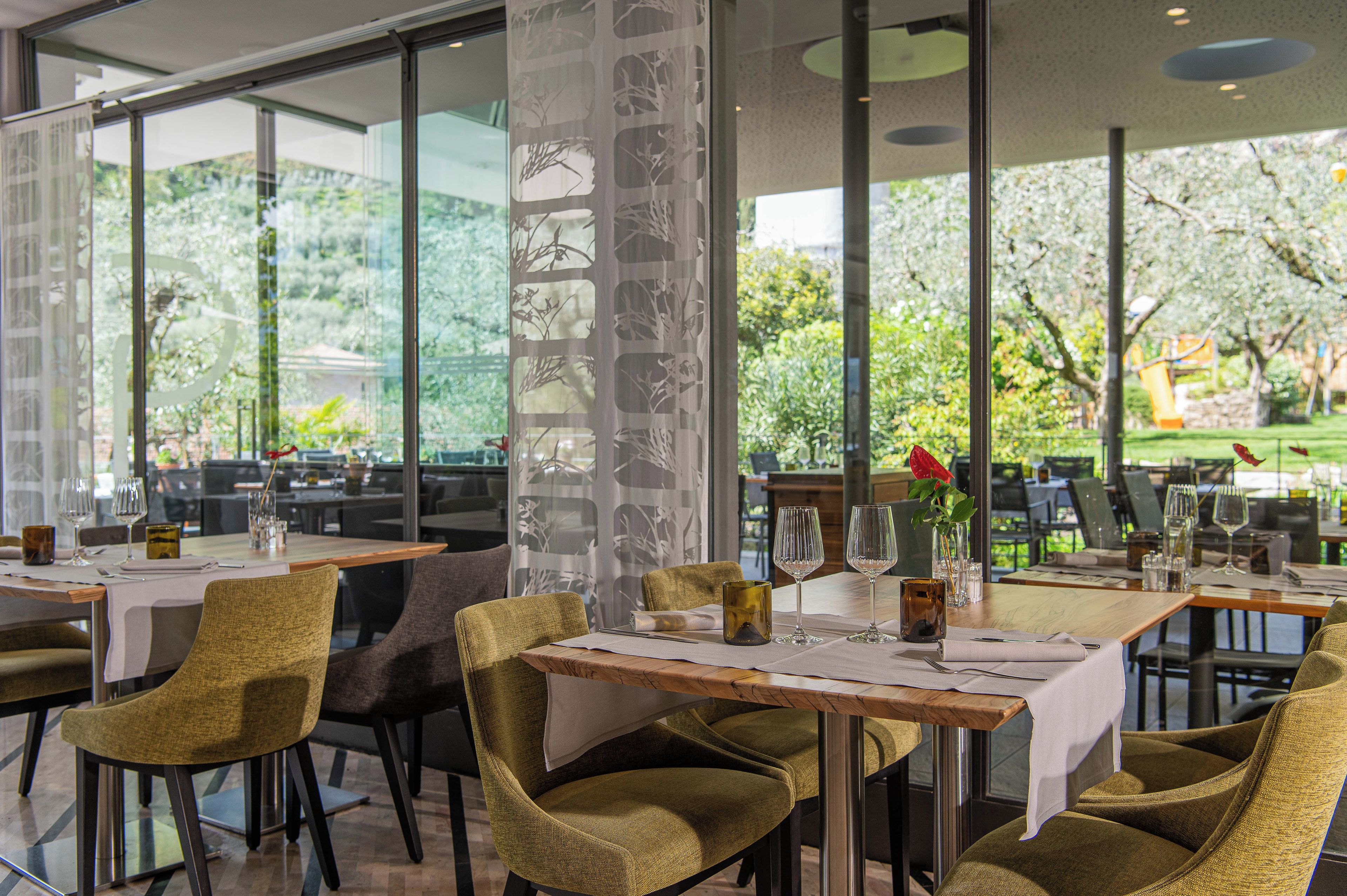 Interior de restaurante com mesas preparadas para refeições, cadeiras e vista para o exterior com vegetação.