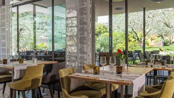 Interior de restaurante com mesas preparadas para refeições, cadeiras e vista para o exterior com vegetação.