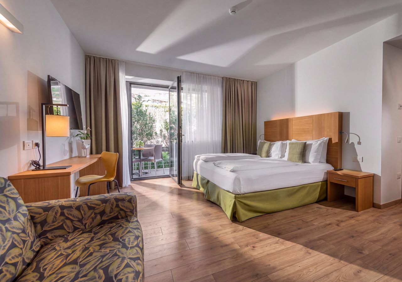 Quarto de hotel com cama, escrivaninha, cadeira e varanda com cortinas.
