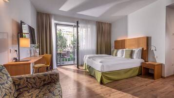 Quarto de hotel com cama, escrivaninha, cadeira e varanda com cortinas.