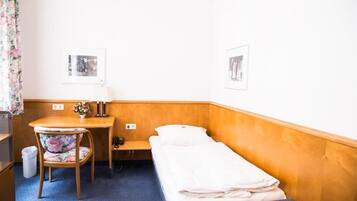 Quarto pequeno com uma cama de solteiro, cabeceira de madeira, escrivaninha com cadeira e duas imagens emolduradas na parede.