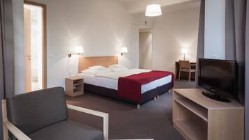 Quarto de hotel com cama, mesas de cabeceira, televisão, escrivaninha e cadeira.