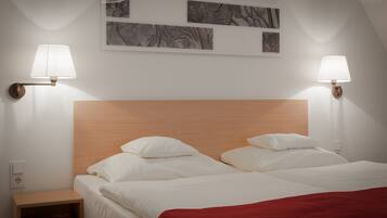 Quarto de hotel com cabeceira de madeira, duas luminárias de apoio, manta vermelha e obras de arte na parede.