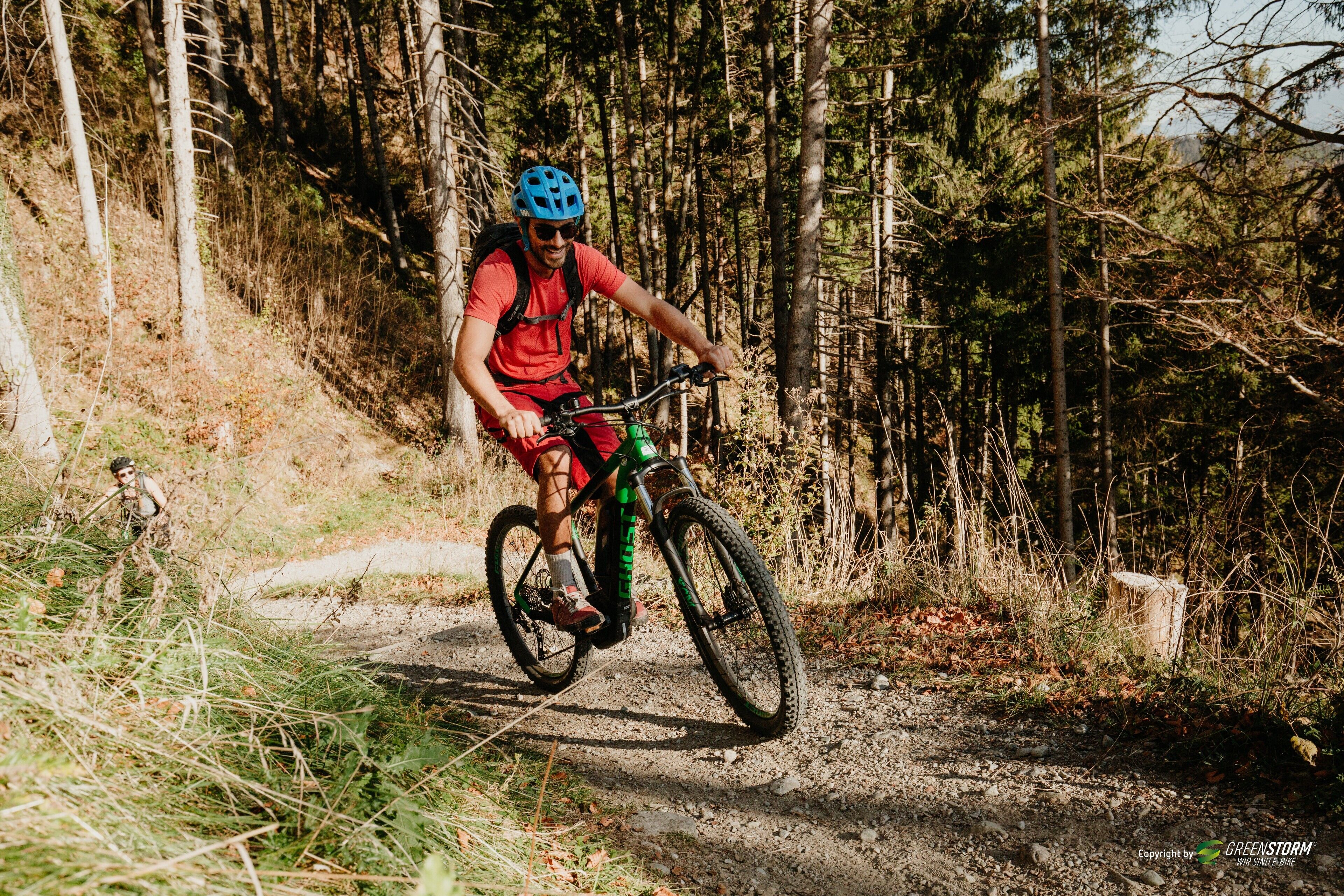 Uma pessoa anda de bicicleta de montanha em uma trilha de terra, cercada por árvores.
