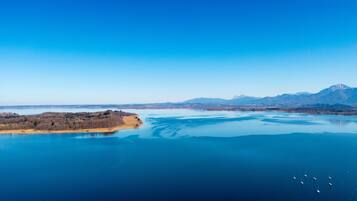 Uma grande extensão de água com barcos, uma área arborizada e montanhas ao fundo.