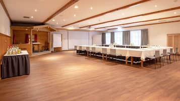 Uma sala de conferências com uma mesa comprida preparada para uma reunião, piso de madeira e estrutura de teto em madeira.