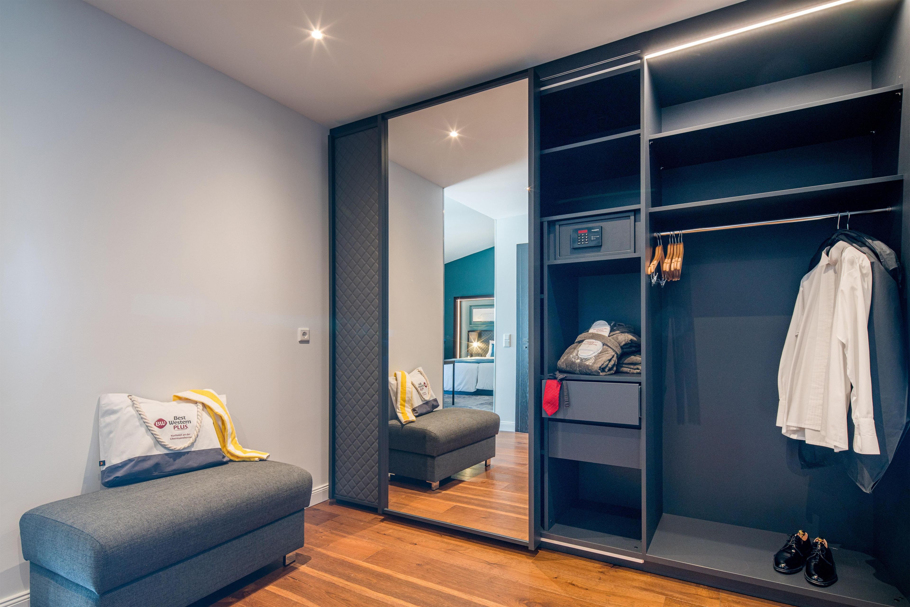 Quarto moderno com sofá cinzento, guarda-roupa espelhado e chão de madeira.