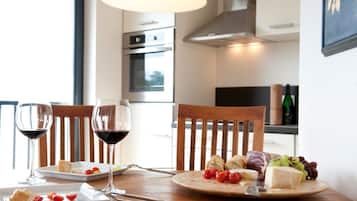 Uma mesa de jantar com copos de vinho, pratos de comida e um tábua de queijos com diversos queijos e uvas.